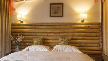 Cama com cabeceira de madeira, dois travesseiros, um quadro emoldurado e duas luminárias fixadas na parede.