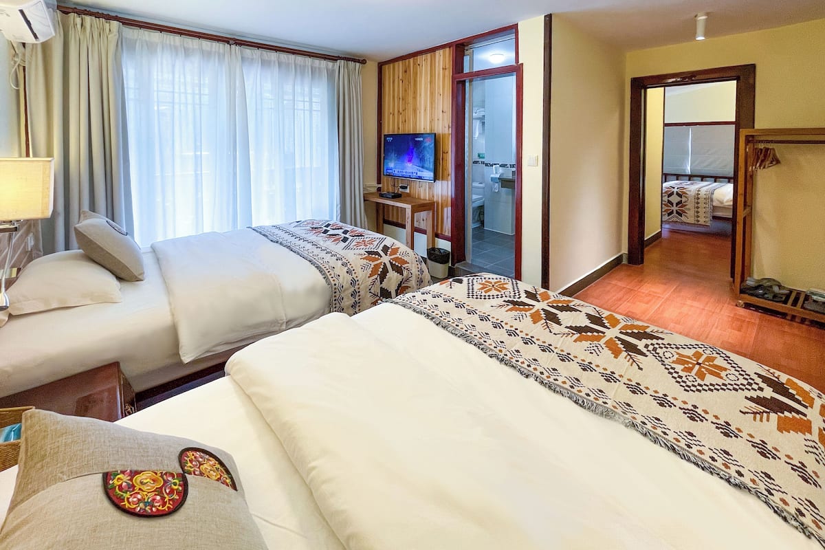 Quarto de hotel com duas camas, televisão e banheiro visível por uma porta aberta.