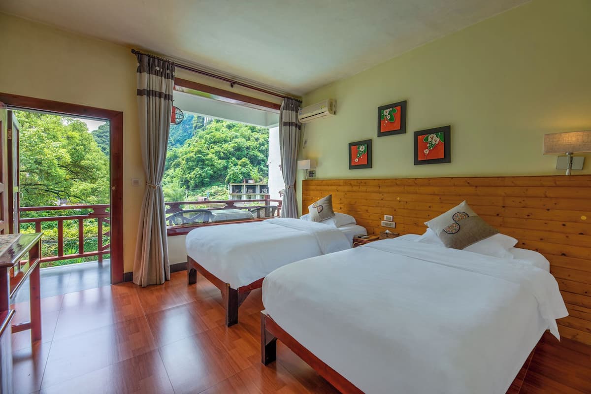 Quarto de hotel com duas camas, uma varanda e vista para vegetação exuberante.
