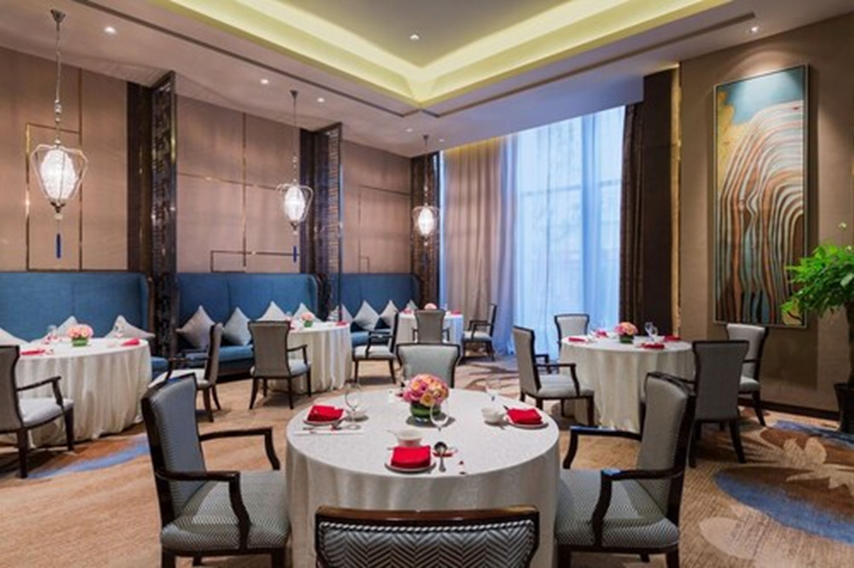 Uma sala de jantar de hotel com mesas redondas, assentos azuis e decoração moderna.