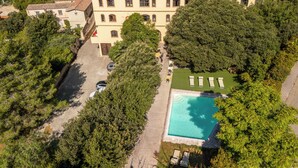 Vista aérea de um edifício grande com piscina, cercado por árvores e área de estacionamento.