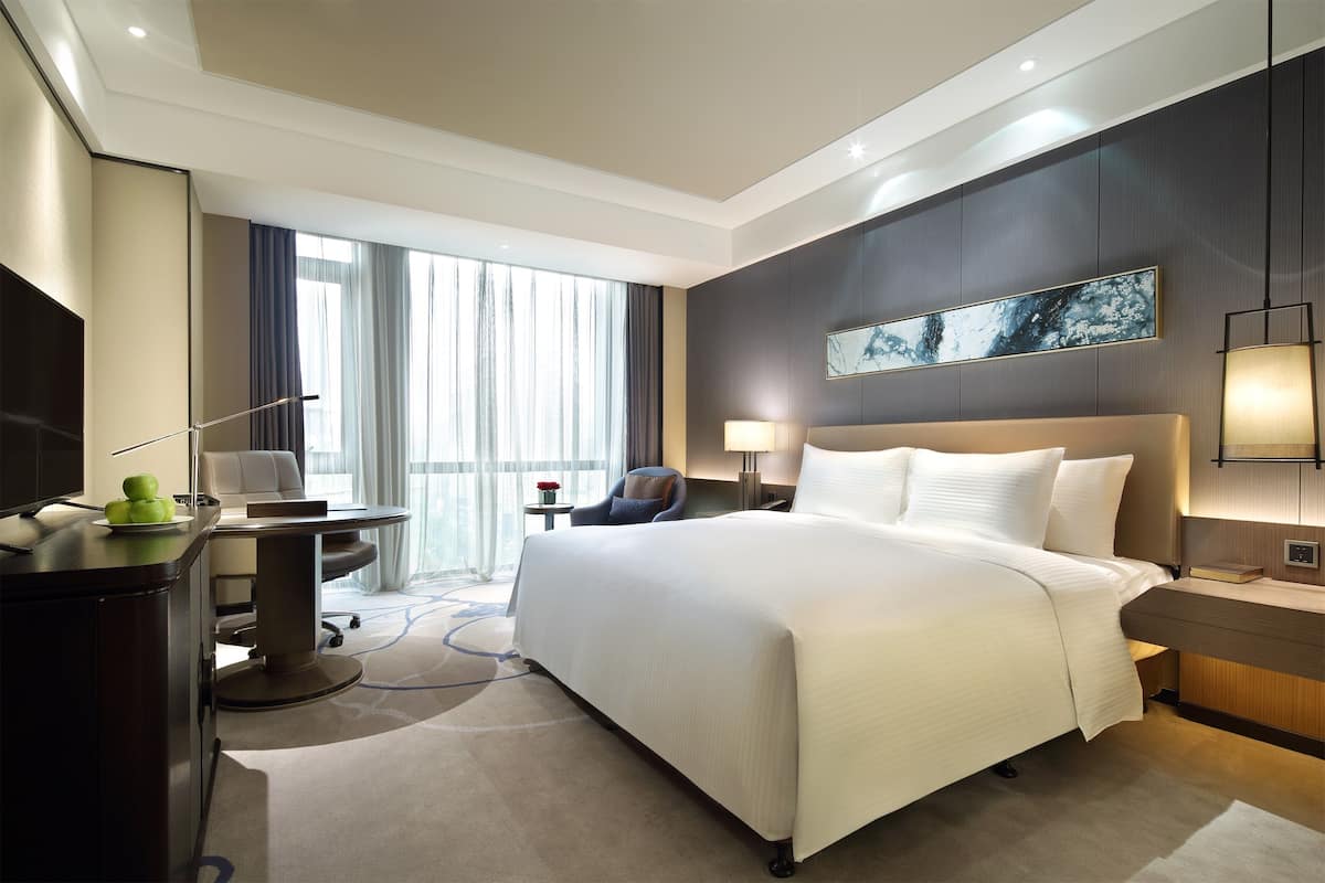 Quarto de hotel com uma cama grande, uma mesa com cadeira, uma televisão e uma janela com cortinas.