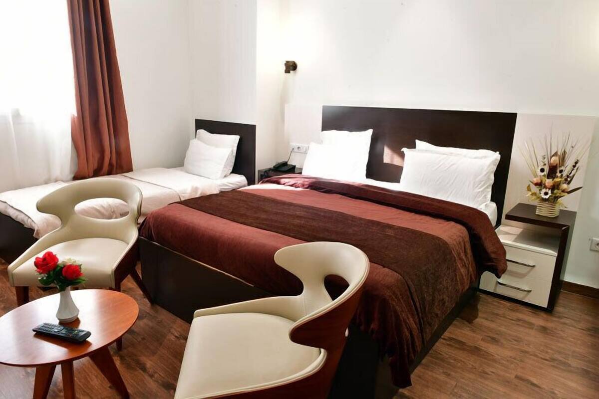 Quarto de hotel com cama, duas cadeiras, uma mesinha com um vaso de flores e uma mesa de cabeceira com abajur.