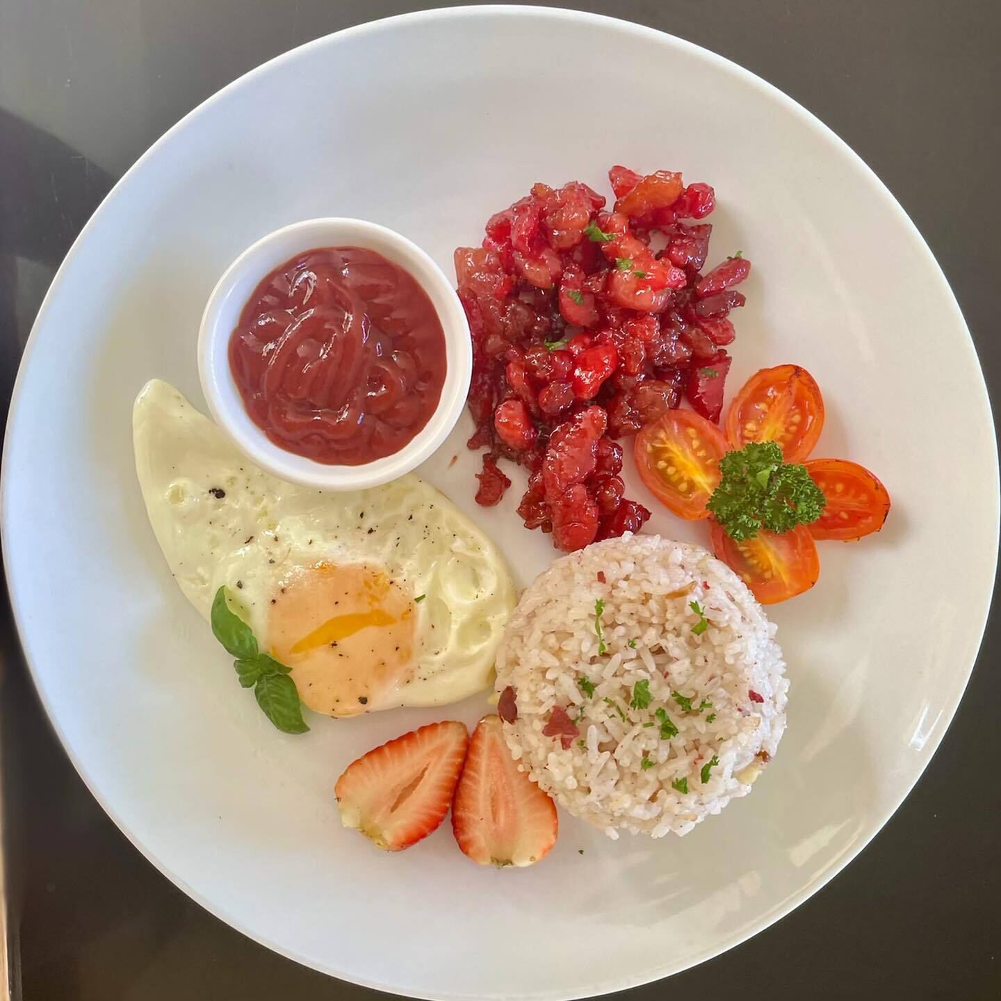 Um prato com ovos mexidos, arroz, morangos, tomates cereja e uma pequena tigela de molho.