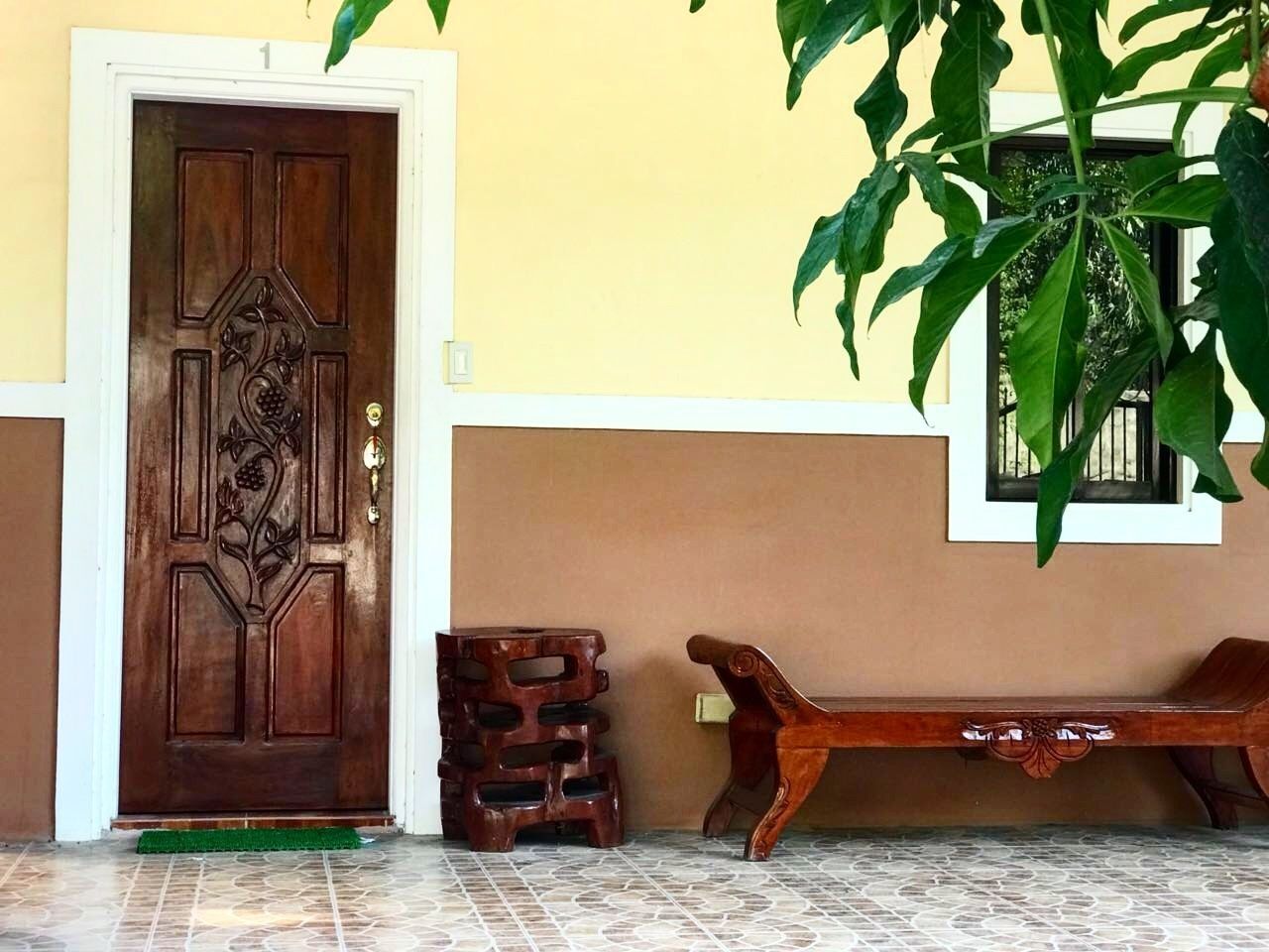 Uma porta de madeira com um painel decorativo, um banco e uma janela com vista para o verde.