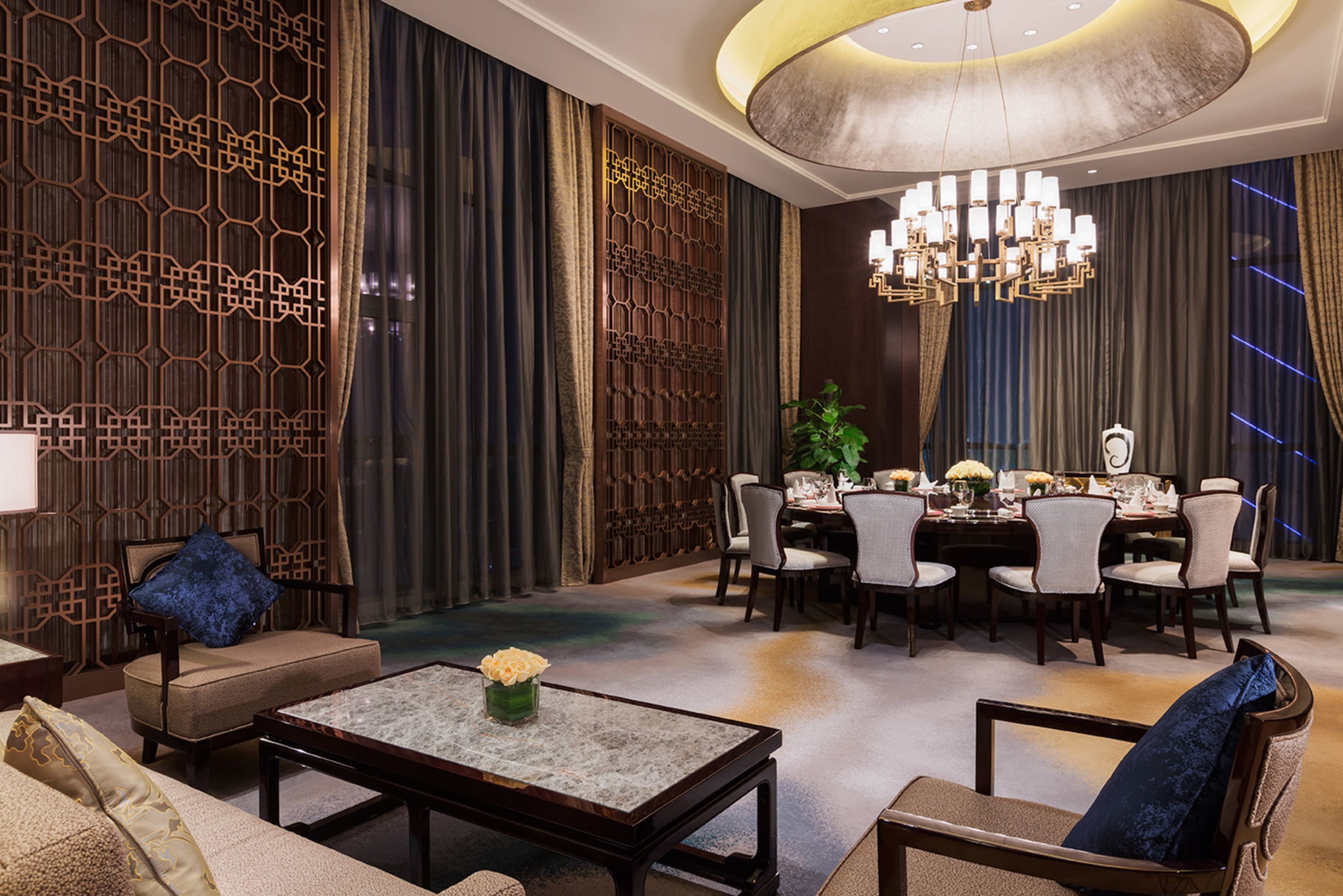 Uma sala de jantar moderna com lustre, mesa, cadeiras e um sofá com almofadas.
