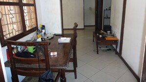 Um quarto com uma mesa de jantar de madeira, cadeiras, uma pequena escrivaninha e um frigorífico ao fundo.