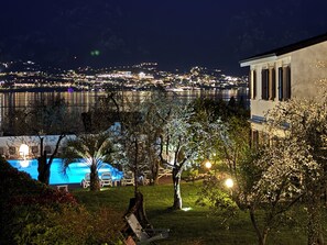 Vista noturna de uma propriedade à beira-mar com piscina, árvores e um edifício com colunas.
