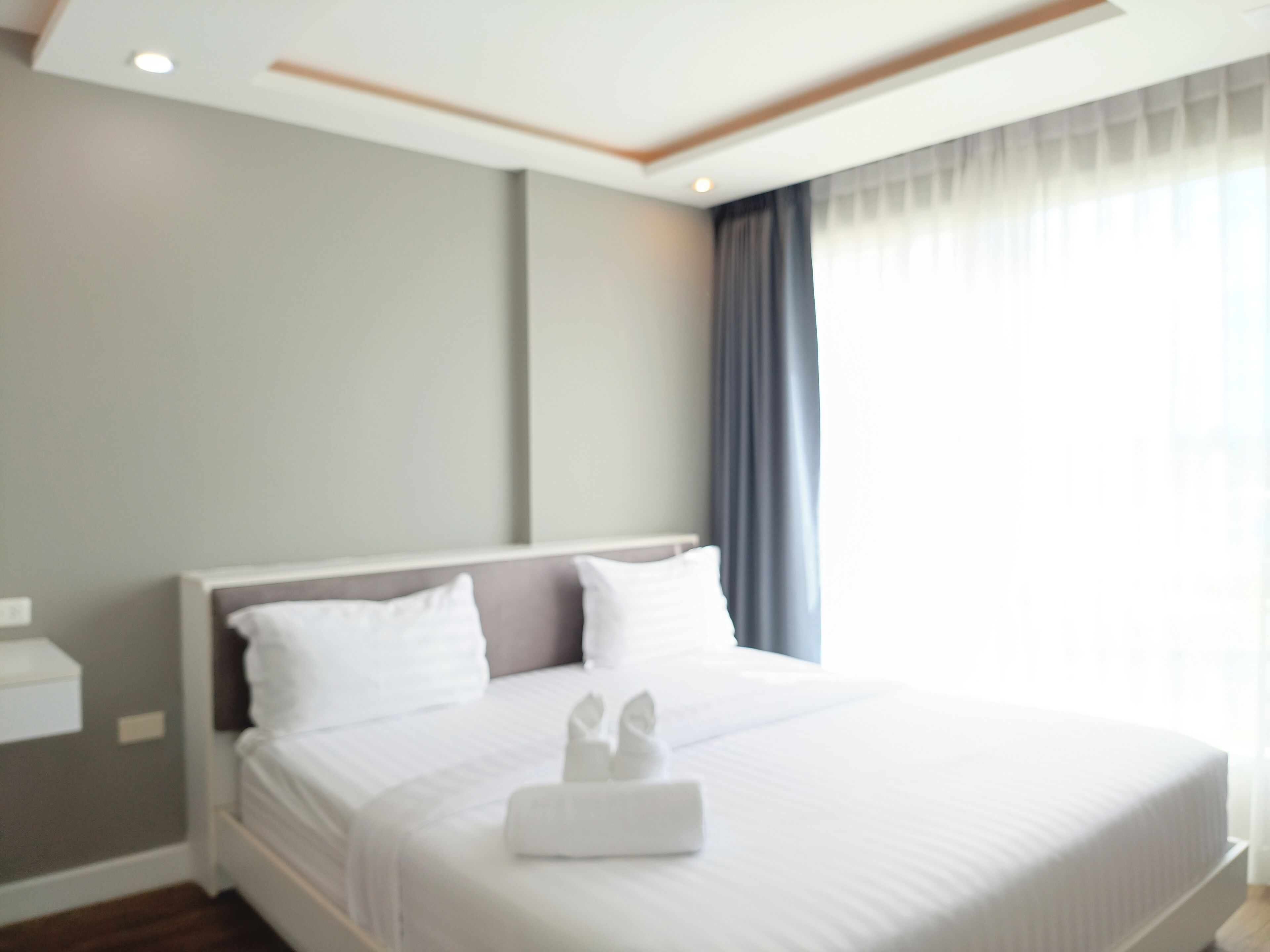 Quarto de hotel moderno com uma cama grande, uma mesinha de cabeceira e uma janela com cortinas.