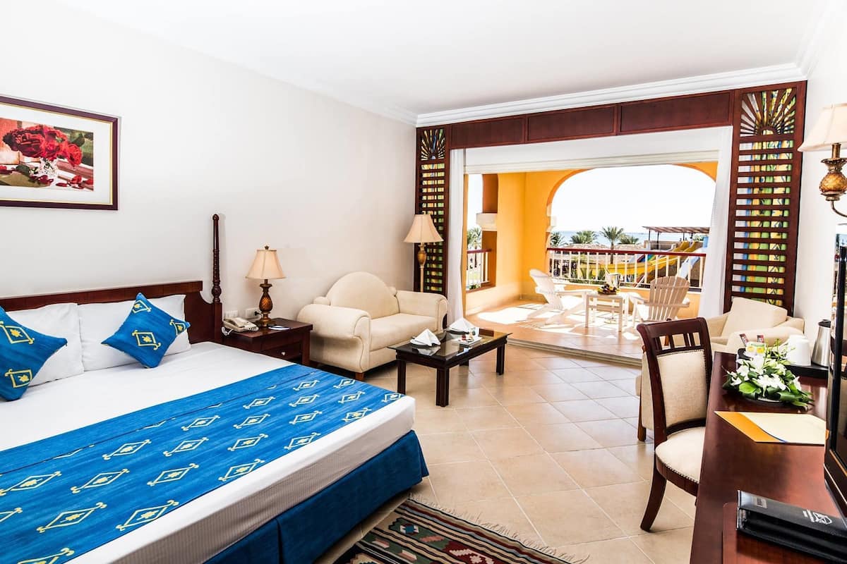 Quarto de hotel com cama, sofá, escrivaninha e varanda com área de estar.