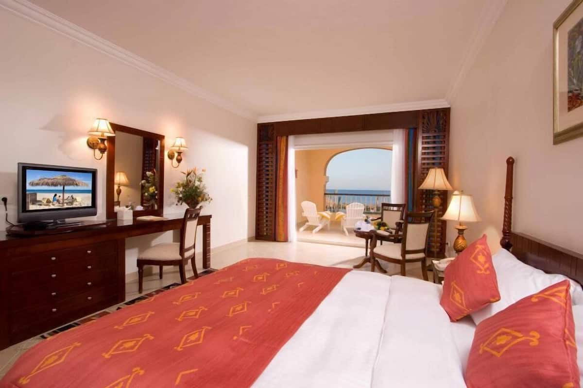 Quarto de hotel com uma cama, uma escrivaninha, uma televisão e vista para o mar.