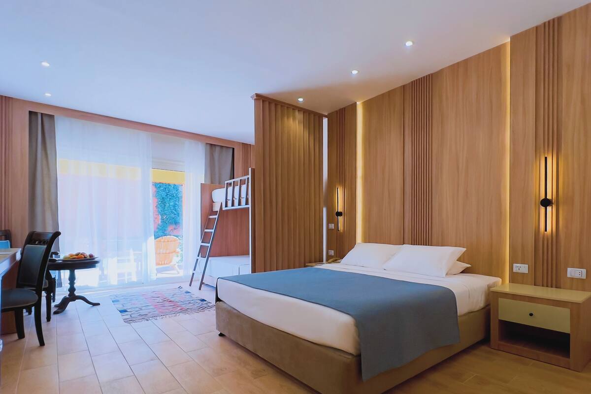 Quarto de hotel moderno com uma cama grande, uma escrivaninha com cadeira e vista para o exterior.