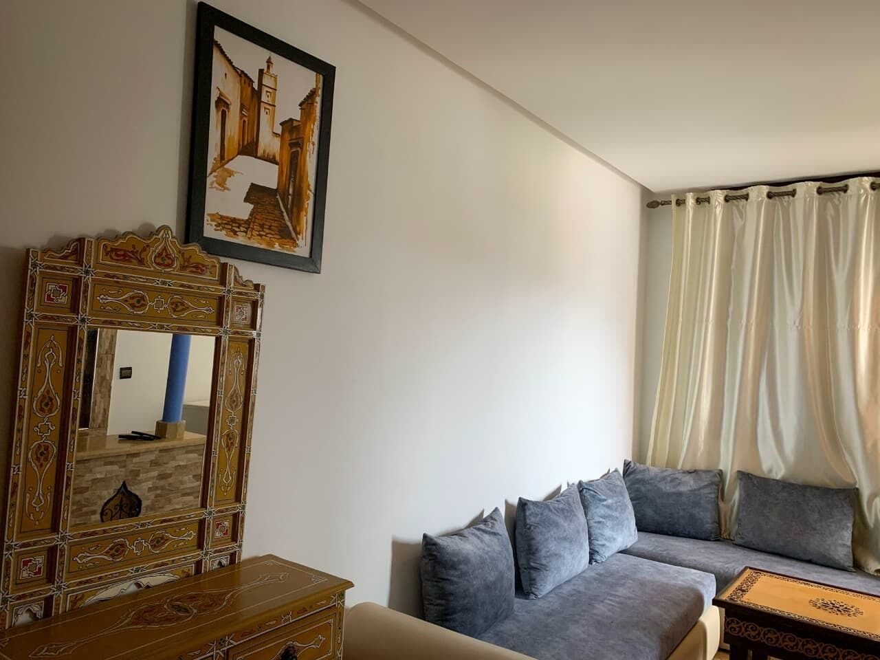Uma sala de estar com um sofá, um armário de madeira, um espelho e um quadro pendurado na parede.