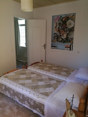 Quarto com cama, porta, estante fixa na parede com livros e um pôster.