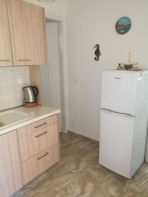 Uma cozinha com armários de madeira clara, bancada branca, chaleira e geladeira branca.