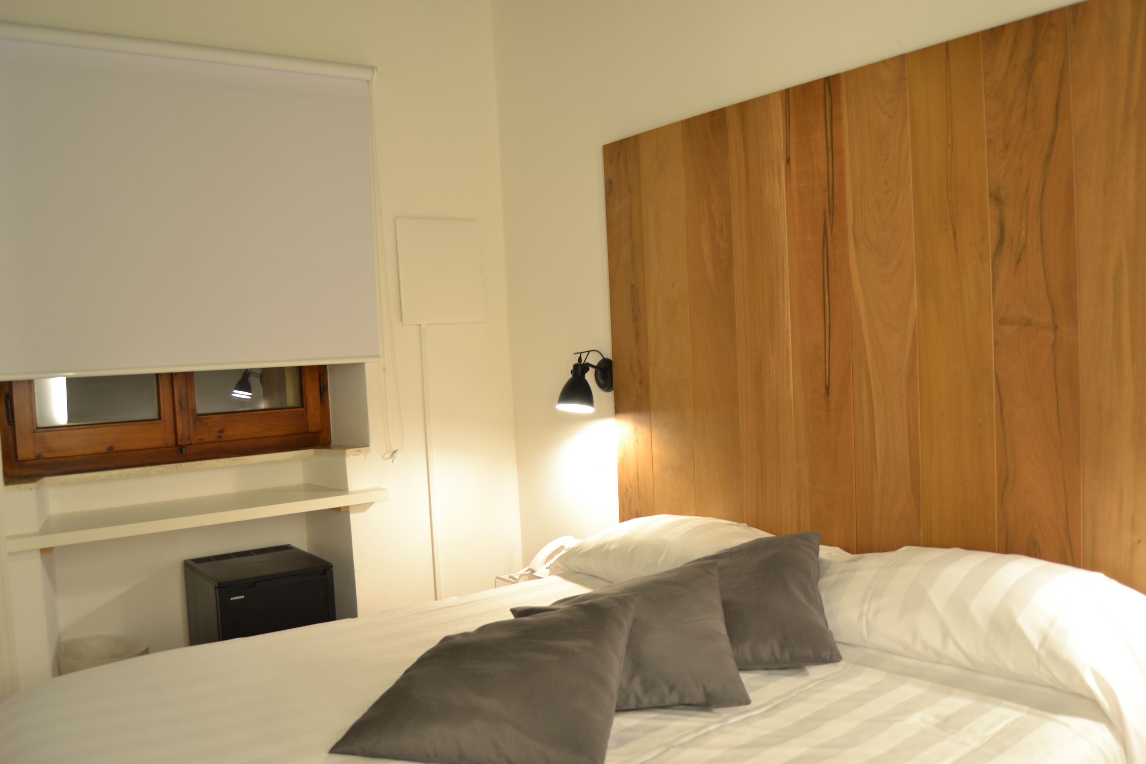 Quarto com cama, almofadas, mesa de cabeceira, abajur e cabeceira de madeira.