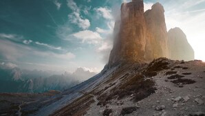 Paisagem montanhosa com terreno rochoso e uma formação rochosa imponente.
