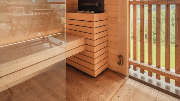 Uma cabana de madeira com sauna, porta de vidro e vista para o exterior.