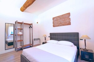 Quarto de hotel com uma cama grande, duas mesas de cabeceira, um guarda-roupa e um espelho.