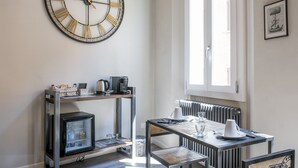 Uma cozinha moderna com um relógio de parede grande, uma geladeira embutida, uma cafeteira e um espaço de jantar com mesa e cadeiras.