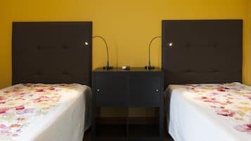 Quarto com duas camas, uma mesinha de cabeceira e um pequeno armário.