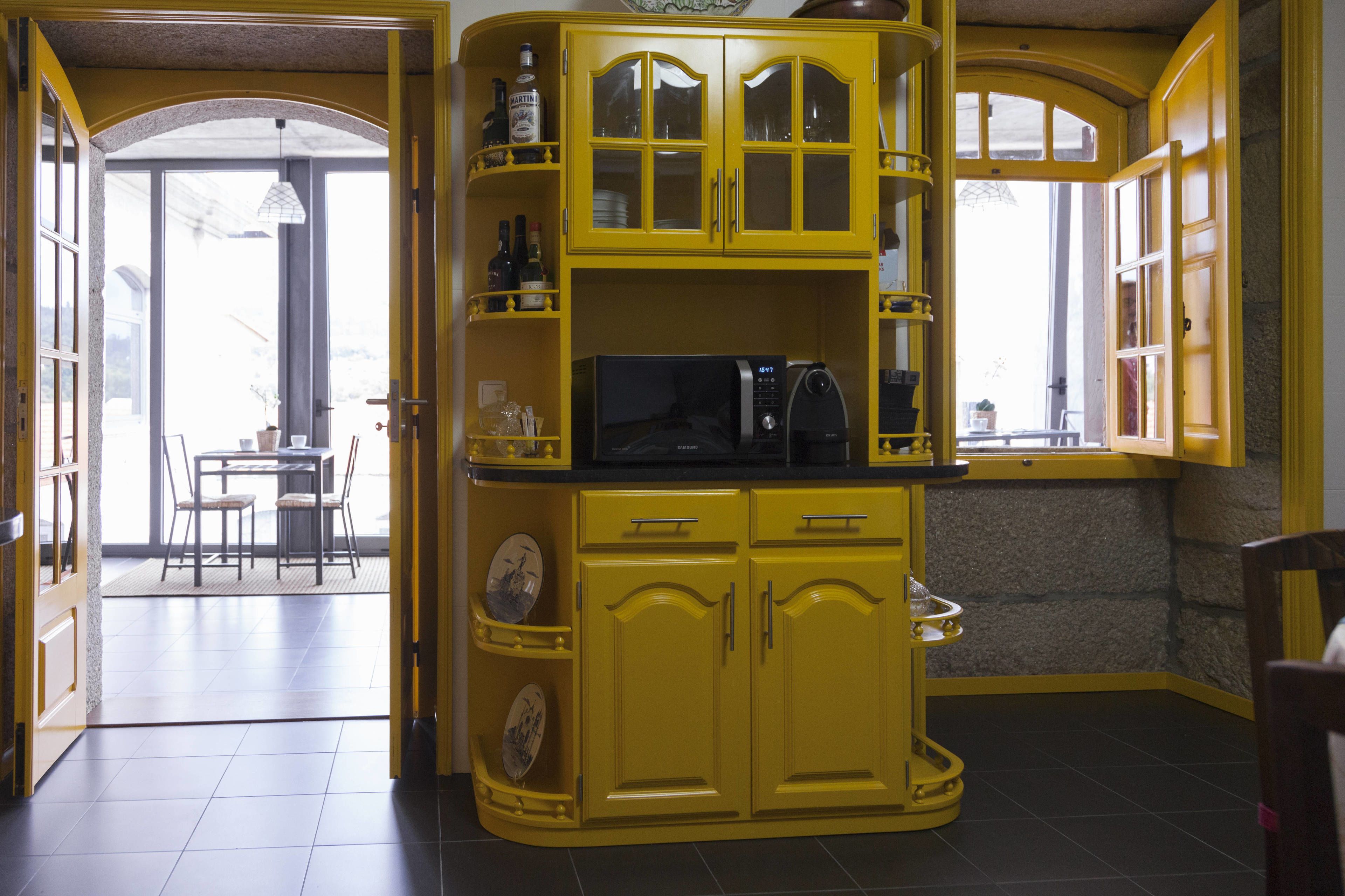 Cozinha amarela com micro-ondas, armários e um espaço de jantar com cadeiras e mesa.