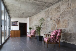Um hall espaçoso com parede de pedra, duas cadeiras de madeira com almofadas estampadas, uma planta em vaso e um quadro na parede.