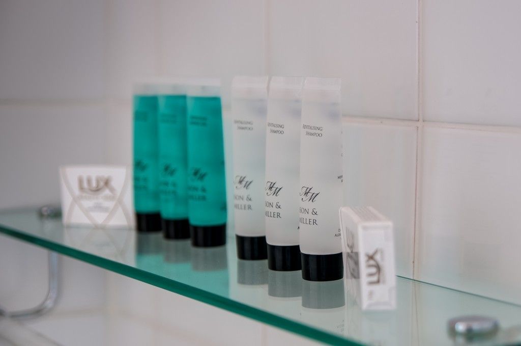 Uma prateleira no banheiro com diversos produtos para cabelo, incluindo frascos e uma caixa.