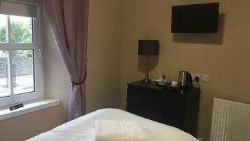 Quarto de hotel com cama, televisão de tela plana na parede, mesa de cabeceira com abajur e janela com cortinas.
