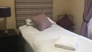 Cama bem arrumada com lençóis brancos, cabeceira listrada e toalha branca dobrada sobre a cama.