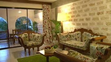 Um quarto com dois sofás de padrão floral, uma mesa de centro de madeira com uma tigela de frutas e uma grande janela com vista para o verde.