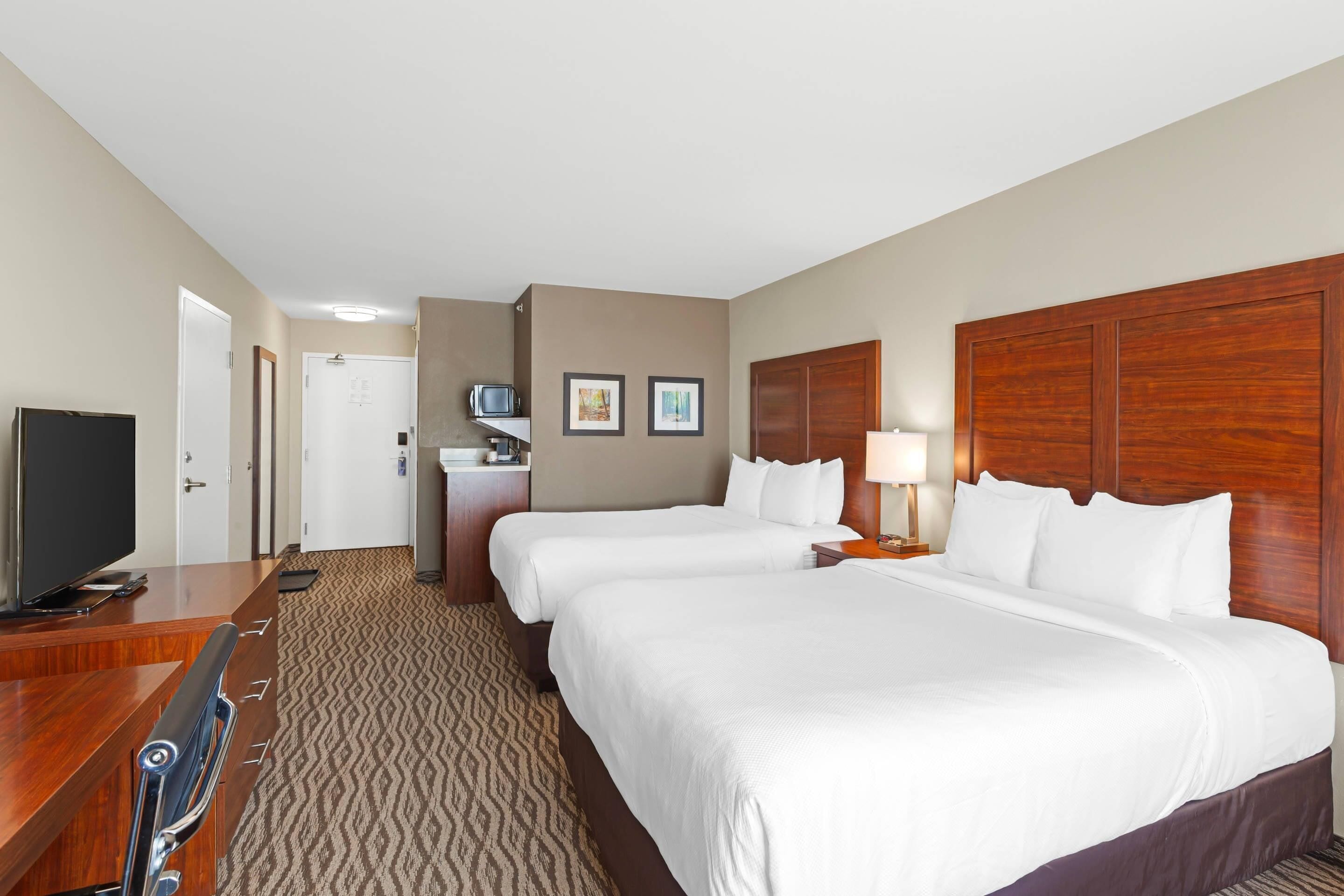 Quarto de hotel com duas camas, uma mesa de trabalho, televisão, minibar e porta de banheiro.