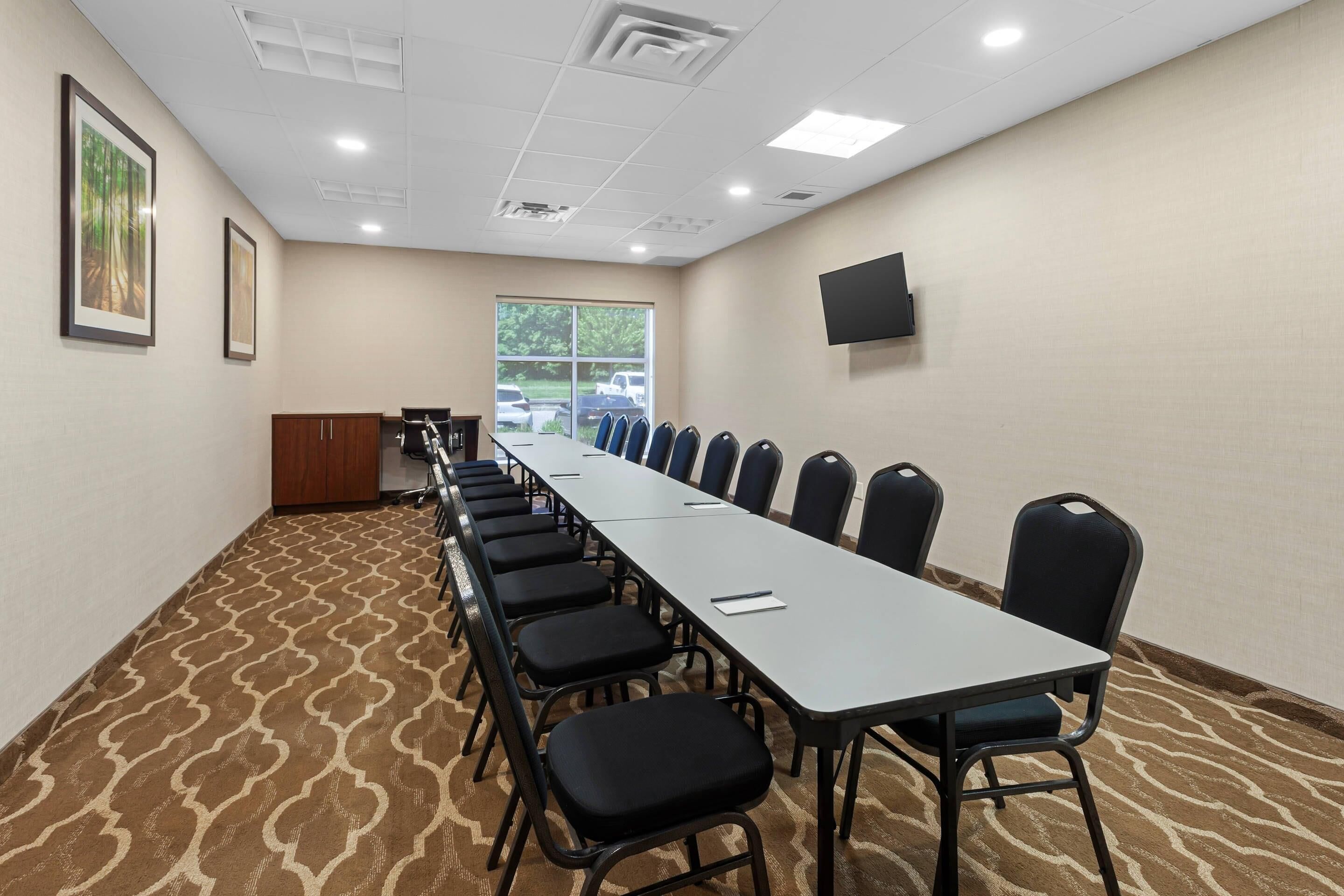 Uma sala de conferências com uma mesa comprida, cadeiras, um pódio e uma televisão na parede.