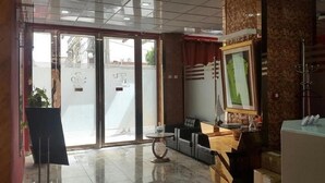 Um saguão de hotel com balcão de recepção, área de estar e uma grande janela com vista para a rua.