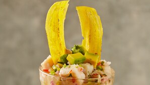Uma saladeira de vidro transparente com salada de mariscos, abacate e cebola vermelha, servida em um prato branco com fundo de mesa de madeira.