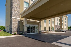 Entrada de hotel com fachada de pedra, uma galeria coberta e estacionamento.