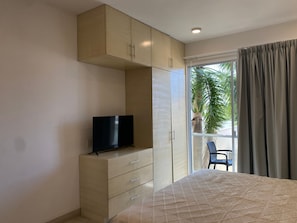 Quarto com uma cama, televisão sobre uma cômoda, janela com cortinas e uma cadeira perto da janela.