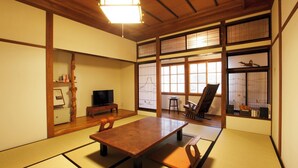 Um quarto japonês tradicional com tatames, uma mesa baixa, uma televisão e portas deslizantes.
