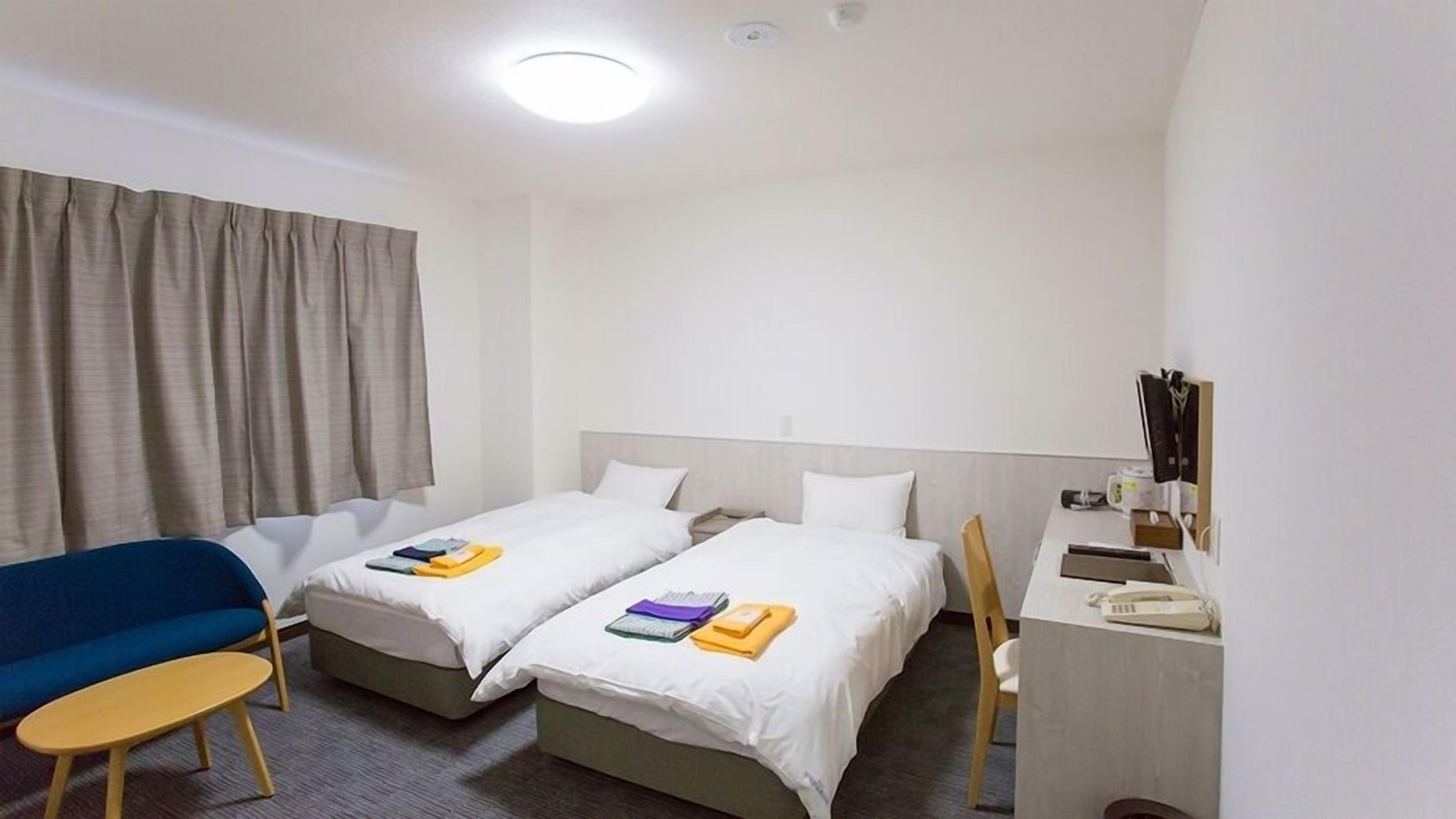 Quarto de hotel com duas camas, uma escrivaninha, uma cadeira e um sofá.