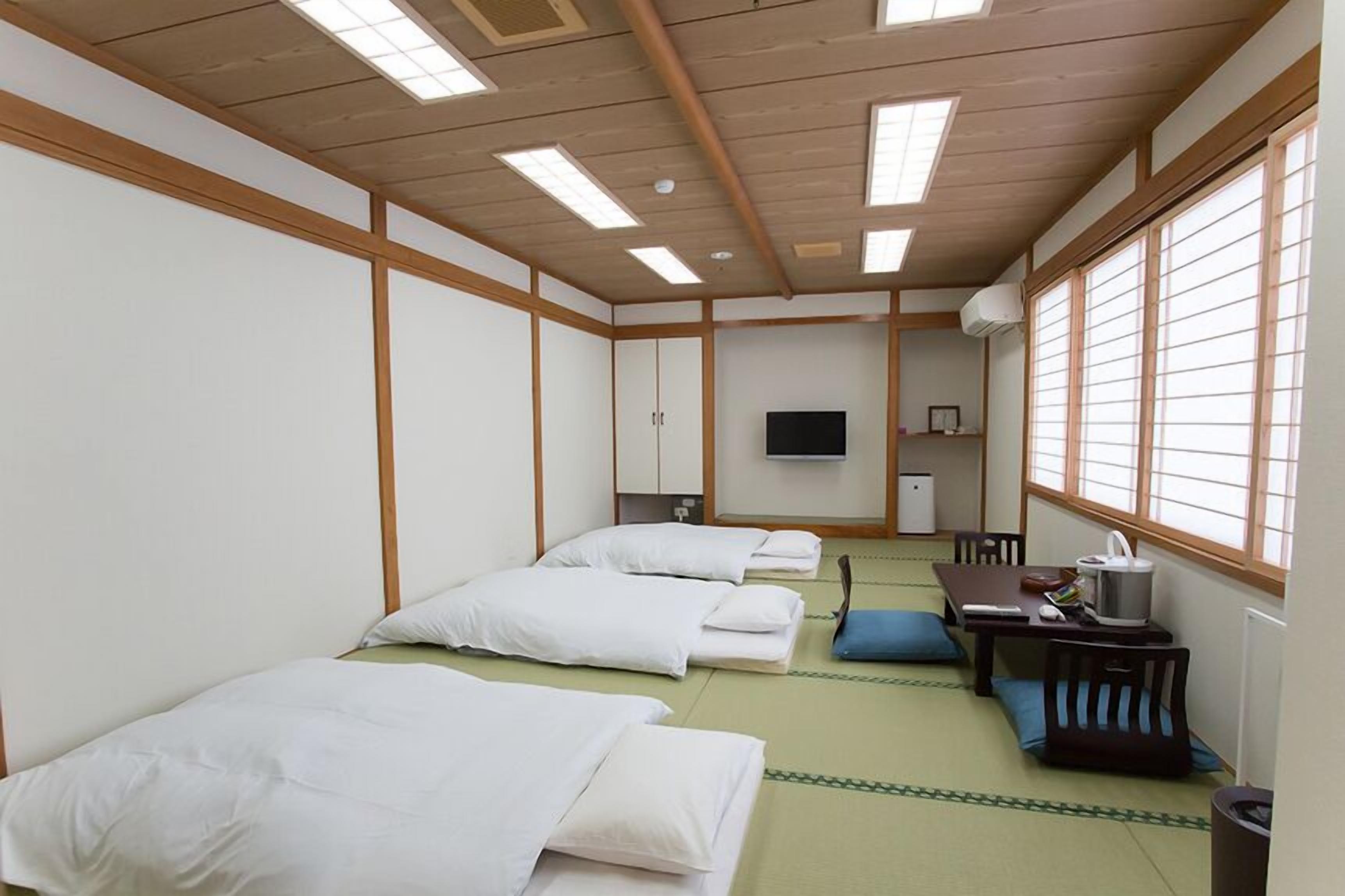 Um quarto japonês tradicional com tatames, futon, televisão e uma escrivaninha com cadeira.