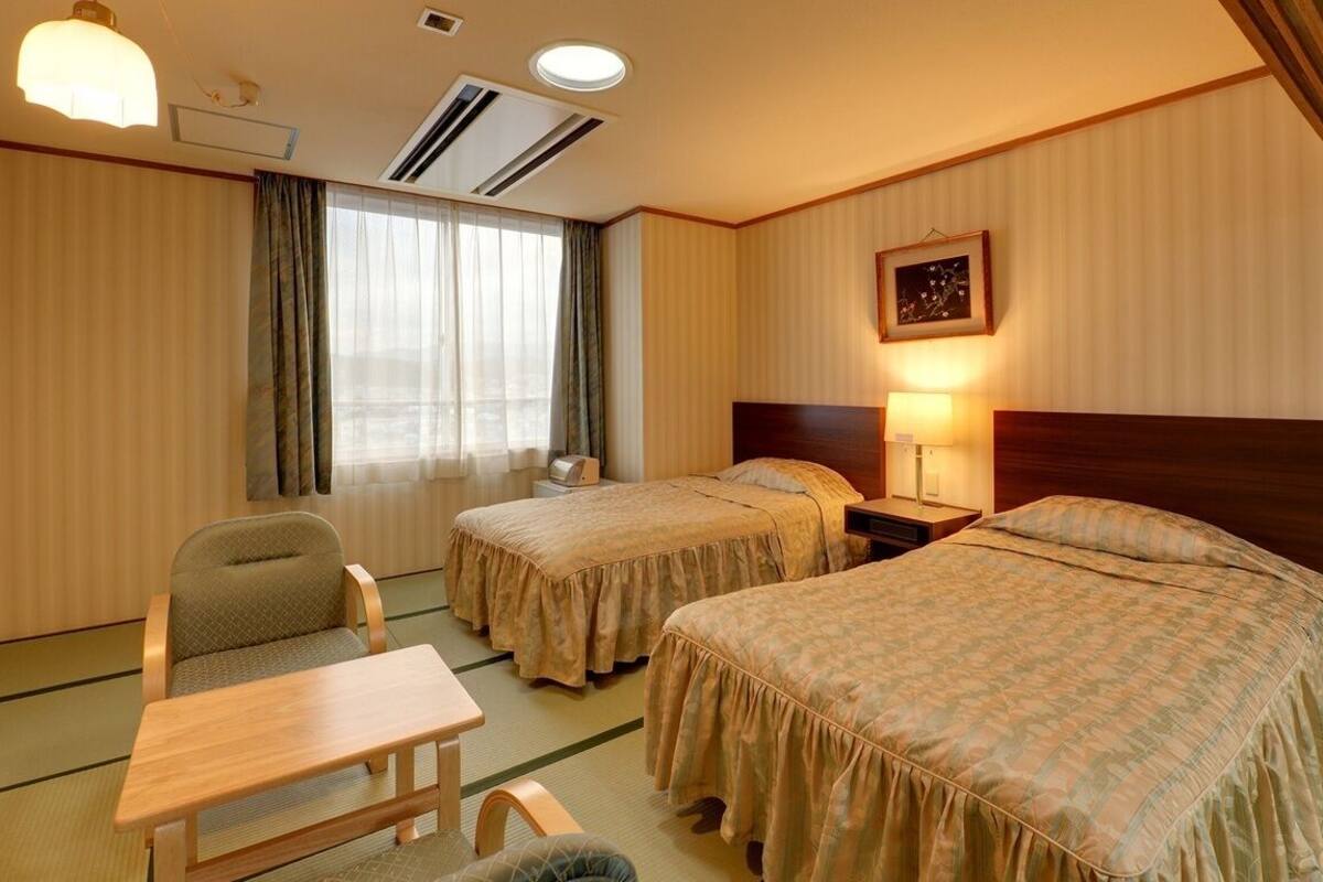 Quarto de hotel com duas camas, uma escrivaninha, uma cadeira, um abajur e um quadro na parede.