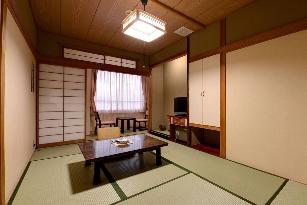 Um quarto japonês tradicional, com tatames, uma mesa baixa, portas de correr e uma televisão.