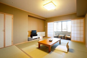 Quarto japonês tradicional com tatames, uma mesa baixa com uma tigela, televisão e portas deslizantes.