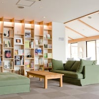 Um espaço de leitura com sofá, mesa de madeira e estantes repletas de livros.