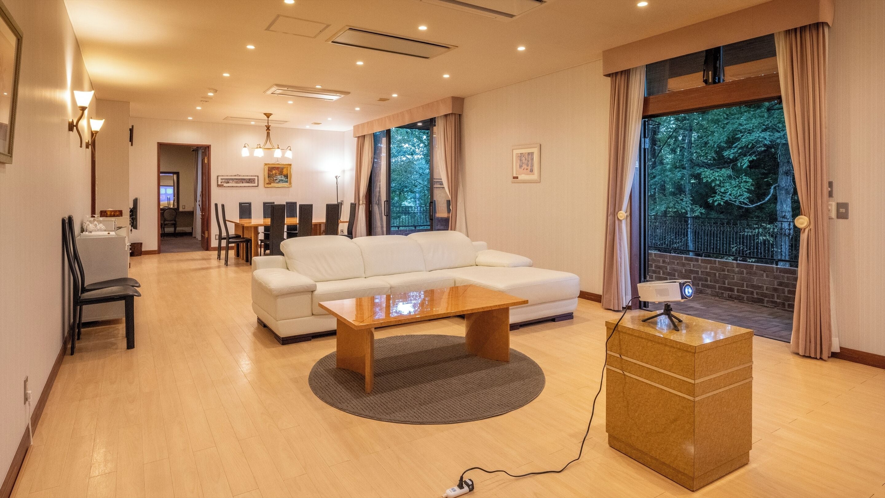 Uma sala de estar espaçosa com um sofá branco, uma mesa de centro de madeira e uma janela grande com vista para o verde.