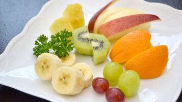 Um prato branco com frutas fatiadas, incluindo bananas, kiwi, maçãs, laranjas e uvas.