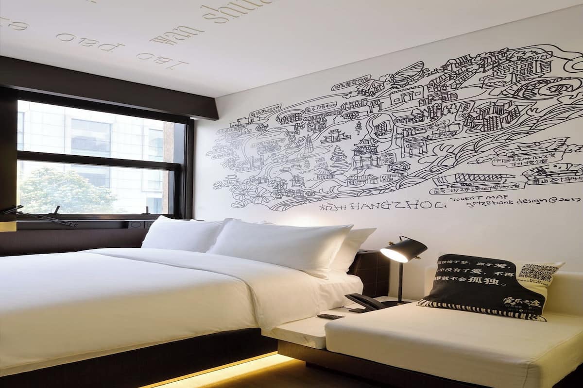 Quarto de hotel com um mapa de parede grande, uma cama, mesa de cabeceira e um pequeno sofá.