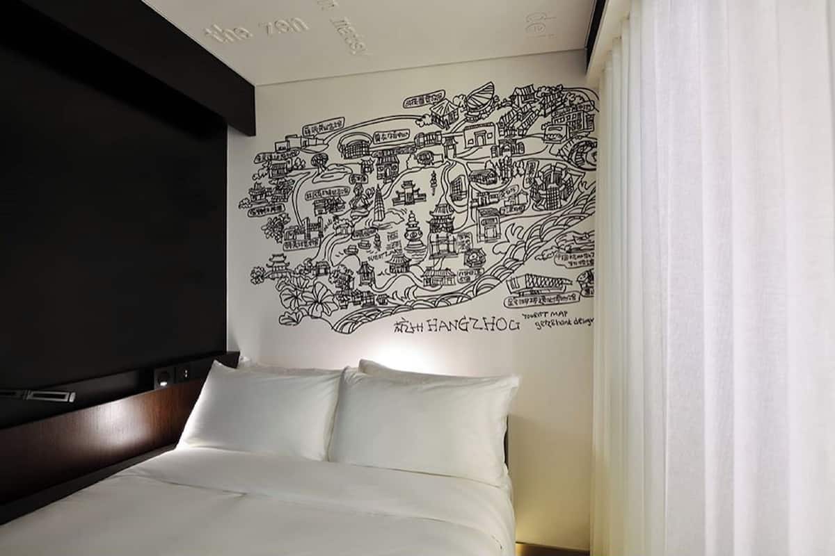 Quarto de hotel com cama, um mural na parede e janela com cortinas.