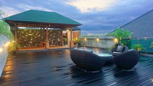 Um pátio moderno ao ar livre com parede de pedra, deck de madeira e duas poltronas confortáveis pretas.