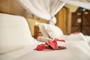 Cama com lençóis brancos, um dossel e um único pétala de rosa vermelha sobre o travesseiro.